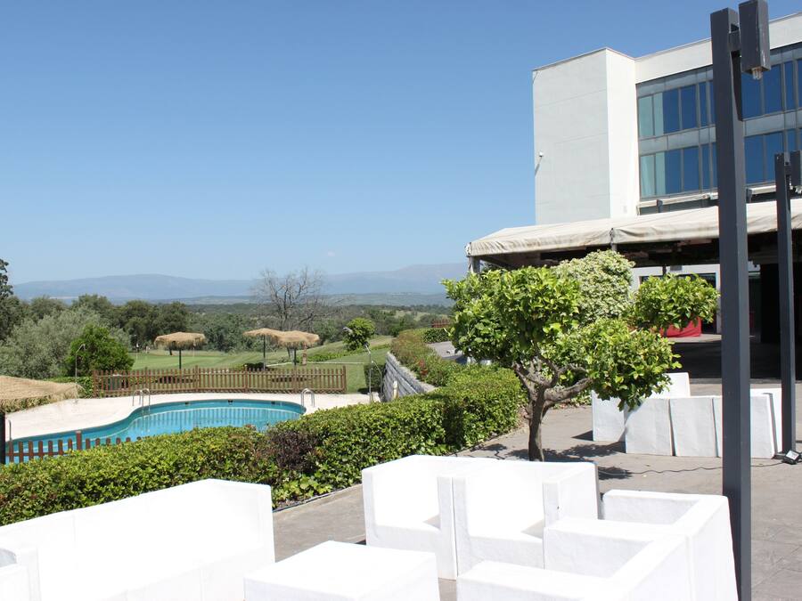 Uma área de piscina com cadeiras de lounge brancas, céu azul límpido e vista para montanhas ao longe.