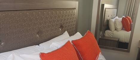 Uma cama bem arrumada com almofadas brancas e listradas, cabeceira texturizada e um espelho refletindo o quarto.