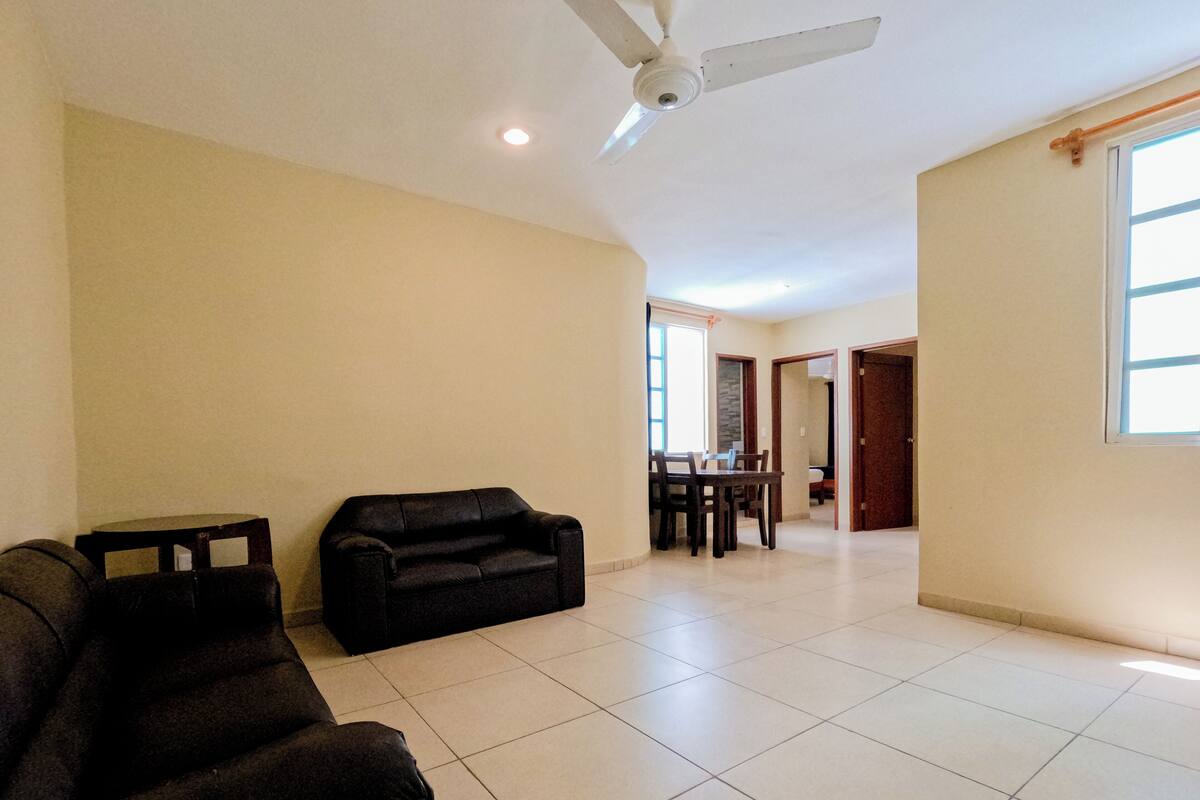 Uma sala de estar ampla com ventilador de teto, uma mesa de jantar com cadeiras e um sofá.