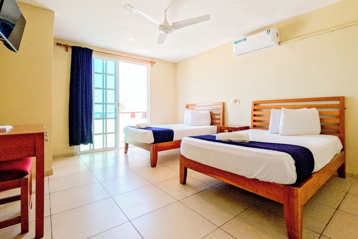 Quarto de hotel com duas camas, ventoinha no teto, ar condicionado, televisão e vista para o exterior.