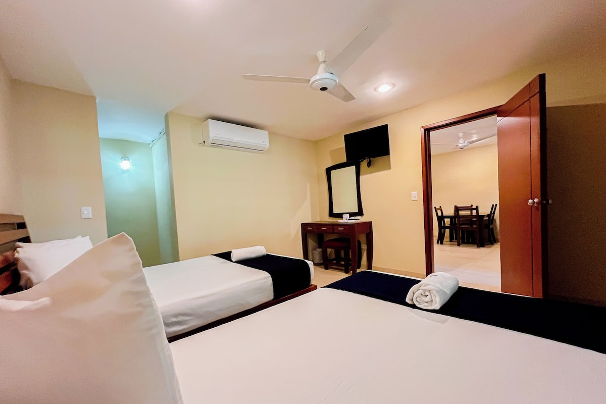 Quarto de hotel com duas camas, uma escrivaninha, uma cadeira, uma televisão e um ar condicionado.