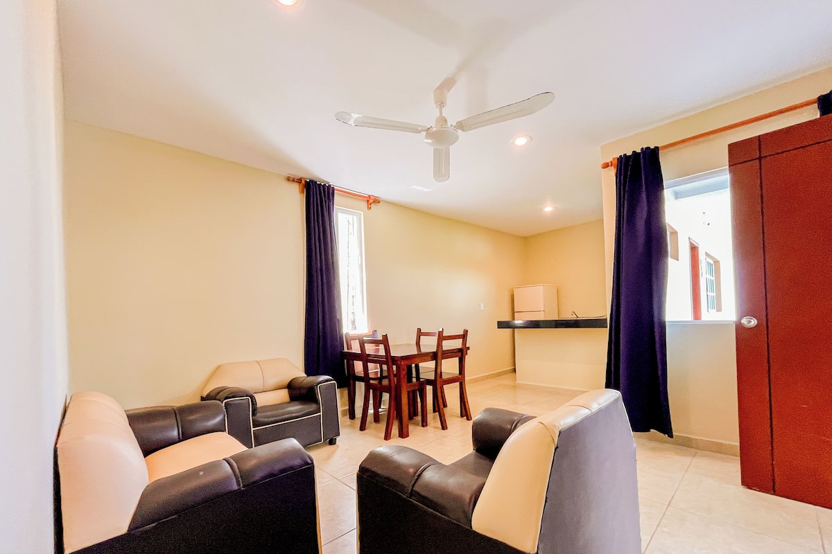 Sala de estar com sofá, cadeiras, mesa de jantar, ventilador de teto e área de cozinha.