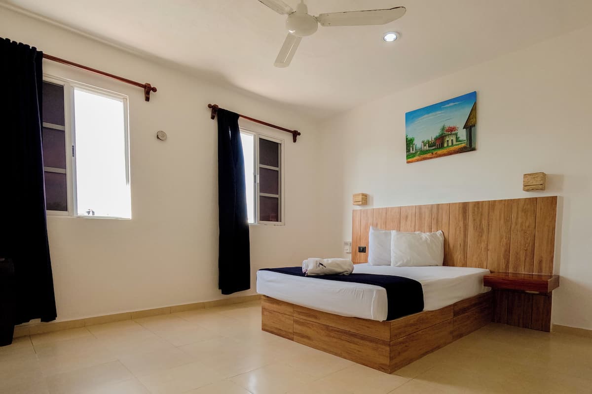 Quarto com cama, ventoinha no teto, um quadro e janela com cortinas.