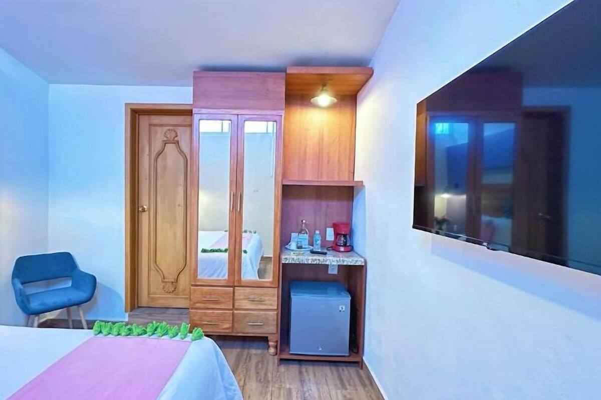 Quarto com cama, guarda-roupa, secretária pequena com luminária e janela.