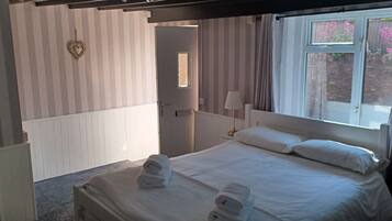 Quarto de hotel com cama, mesa de cabeceira, luminária, janela com cortinas e porta.