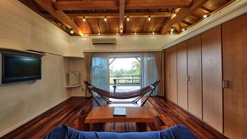 Quarto com teto de madeira, TV de tela plana, rede, mesa e vista para o exterior.