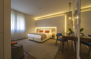 Quarto de hotel moderno com uma cama grande, uma mesa de jantar e uma pequena mesa lateral.