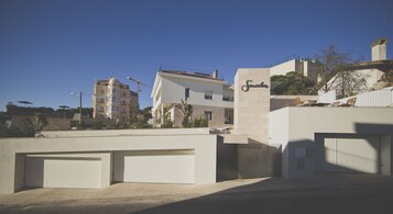 Um edifício residencial moderno com telhado plano, varanda e entrada com portão.
