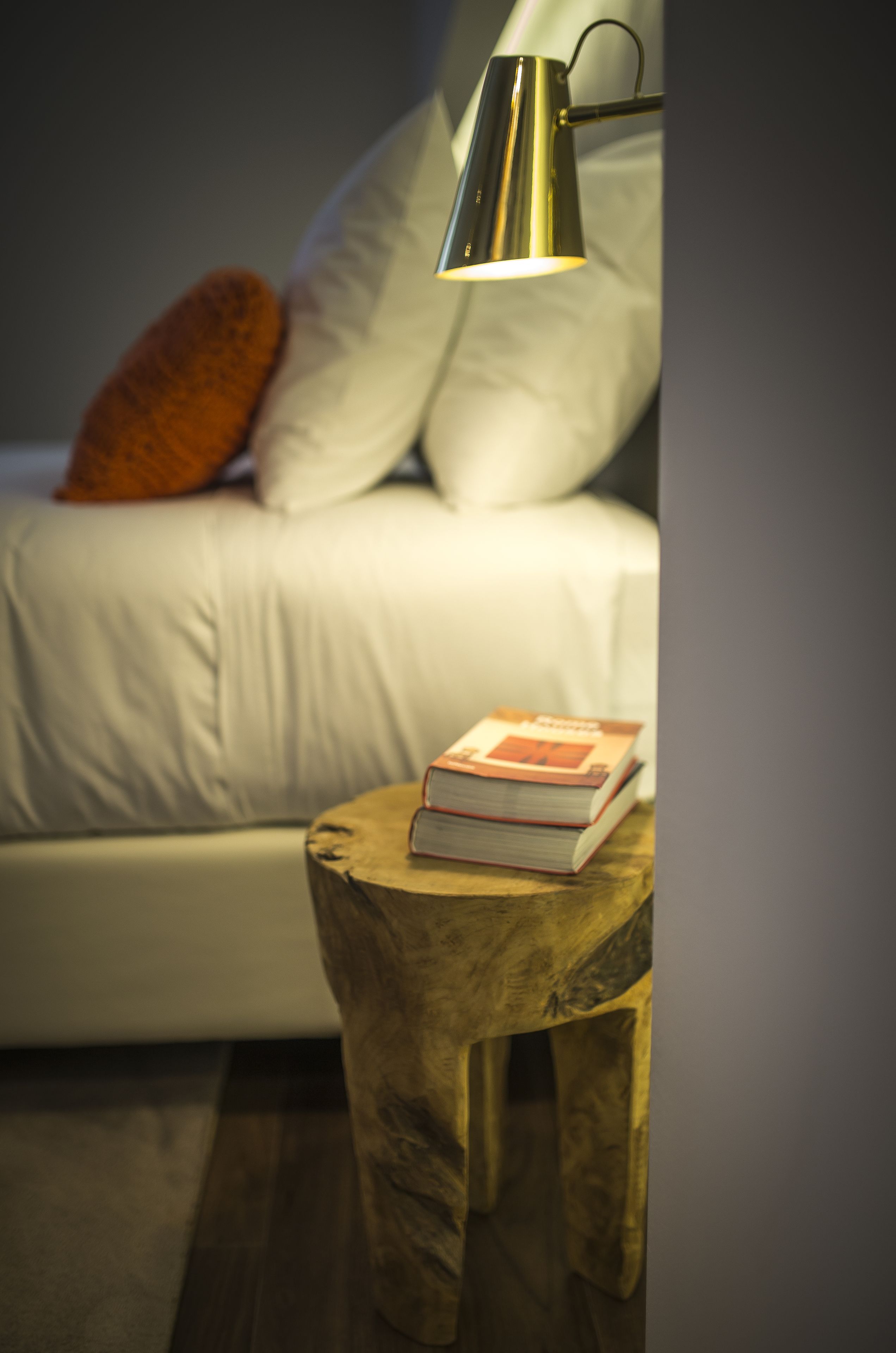 Quarto moderno com cama branca, mesa de cabeceira de madeira e uma luminária.