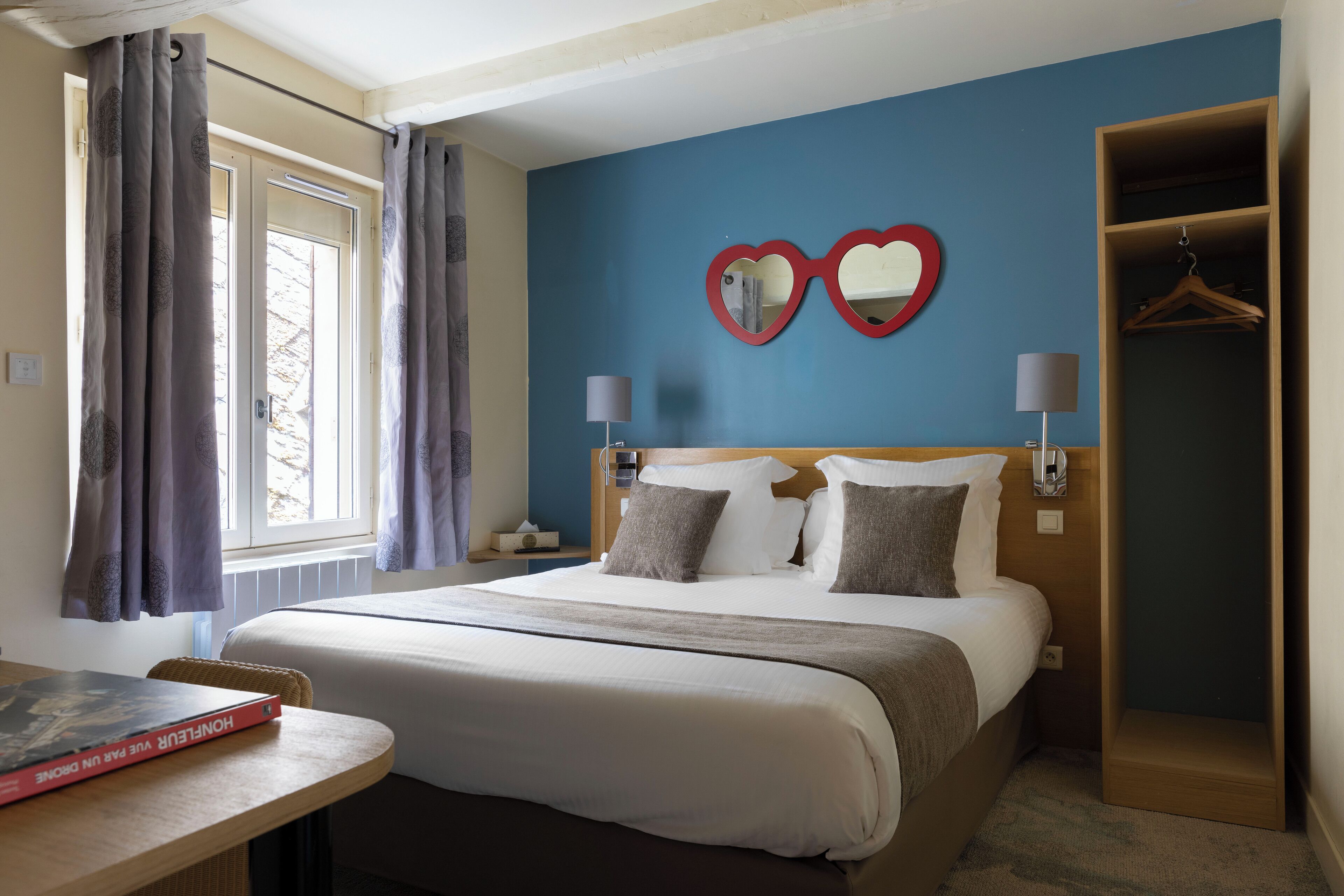 Quarto de hotel com cama, mesas de cabeceira, guarda-roupa e janela com cortinas.