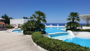 Área de piscina do resort, com palmeiras, espreguiçadeiras e vista para o mar.