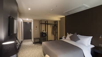 Quarto de hotel com uma cama grande, mesa de cabeceira, luminária, guarda-roupa e espelho.