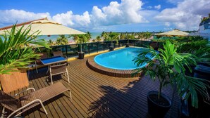 Uma área de piscina com deck de madeira, espreguiçadeiras e guarda-sóis.