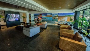 Um hall espaçoso com uma grande televisão de tela plana, assentos confortáveis, um mural na parede com uma cena de praia e plantas em vasos.