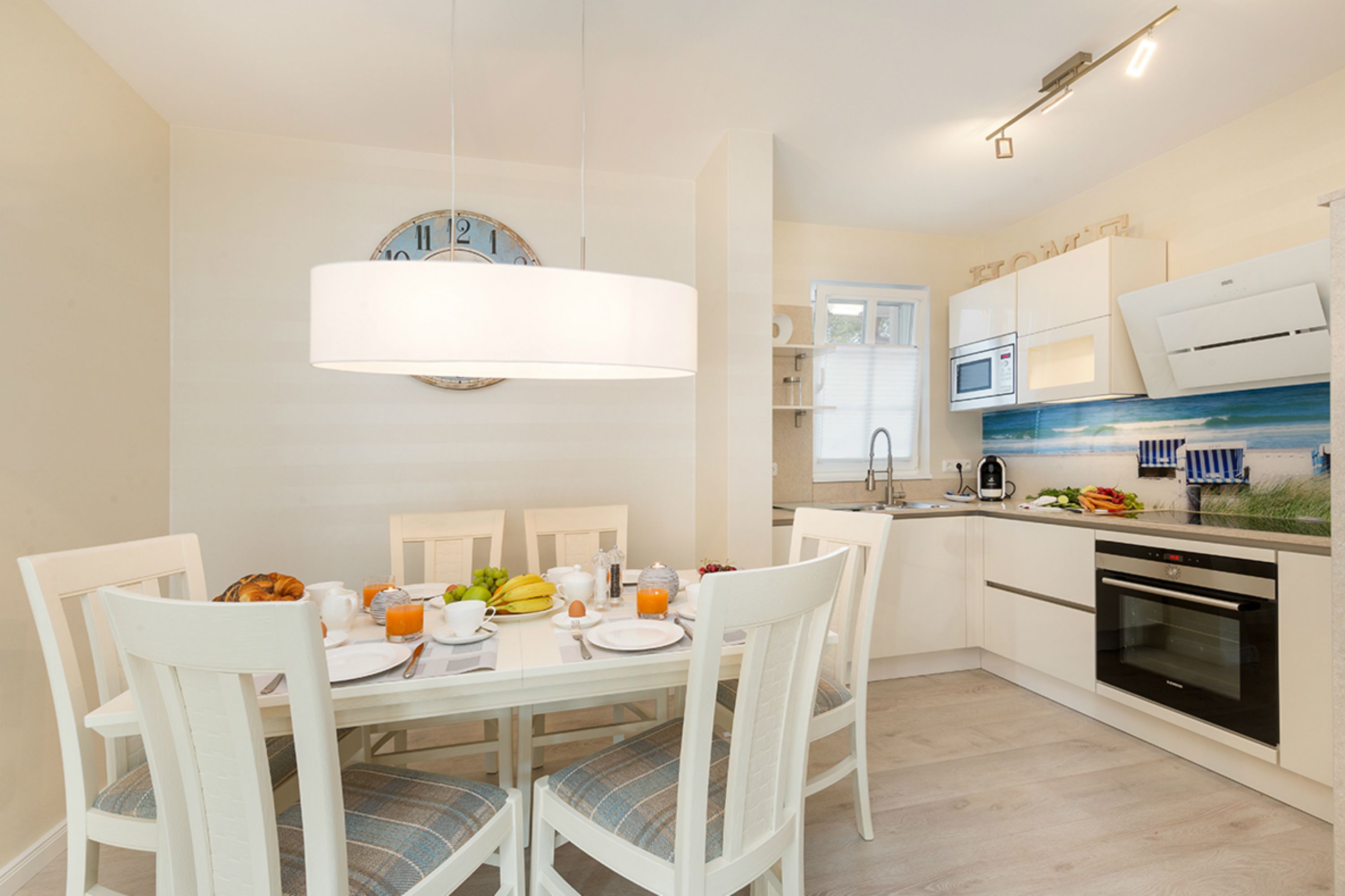 Uma cozinha moderna com armários brancos, uma mesa de jantar com cadeiras, um relógio e um micro-ondas.