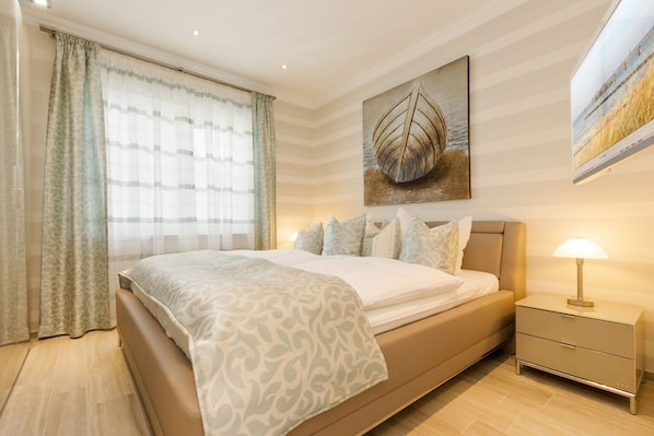 Quarto moderno com uma cama grande, mesa de cabeceira, luminária e obras de arte nas paredes.