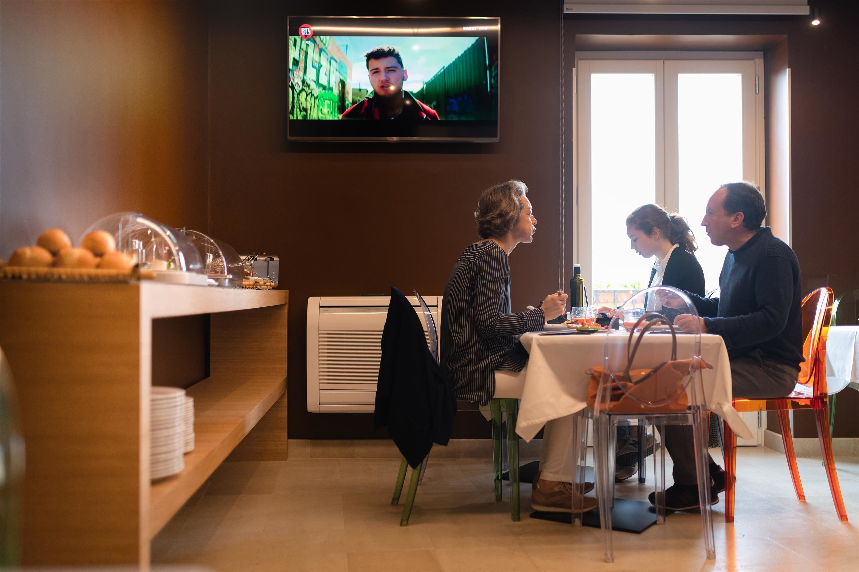 Uma área de refeições com televisão na parede, um buffet com doces, e uma janela que oferece luz natural.