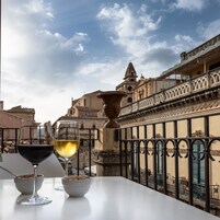 Uma mesa com dois copos de vinho e uma tigela de cereais, com vista para um edifício histórico com varandas elaboradas e uma torre.