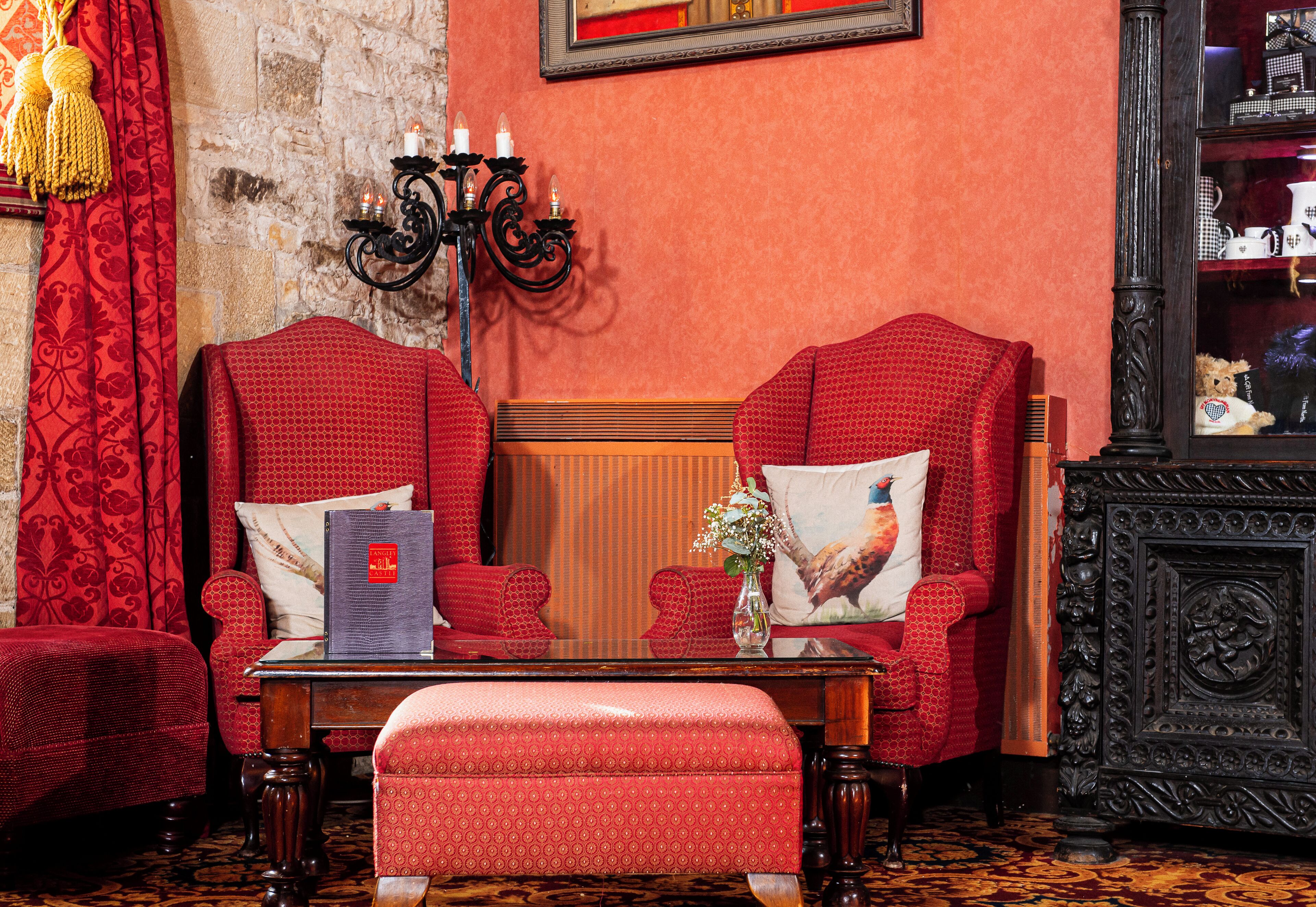 Um quarto com duas poltronas vermelhas estofadas, uma mesa pequena com um vaso e um armário de madeira com detalhes entalhados.