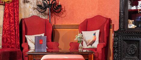 Um quarto com duas poltronas vermelhas estofadas, uma mesa pequena com um vaso e um armário de madeira com detalhes entalhados.