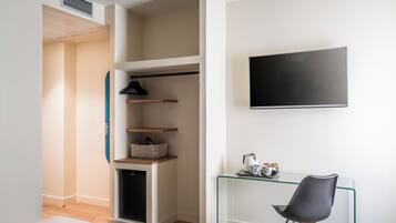 Quarto moderno com cama, mesa de vidro com uma cadeira, televisão e um guarda-roupa embutido com prateleiras.