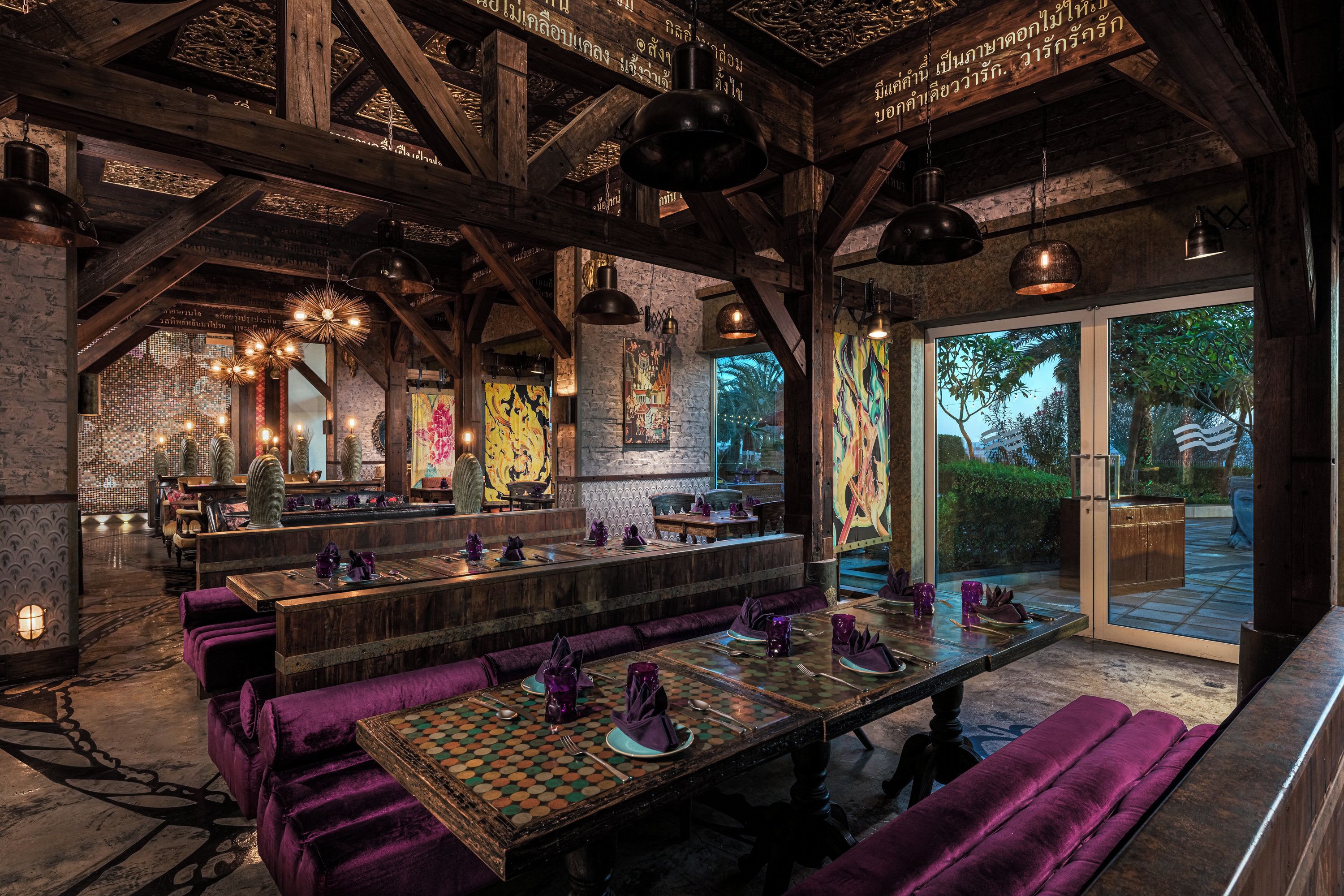 Restaurante com vigas de madeira, uma mesa comunitária grande e assentos roxos.