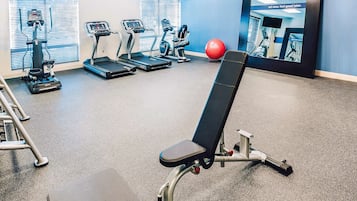 Uma academia com equipamentos de ginástica, um banco e uma bola de exercícios vermelha.