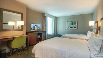 Quarto de hotel com cama, escrivaninha, cadeira, televisão e espelho.