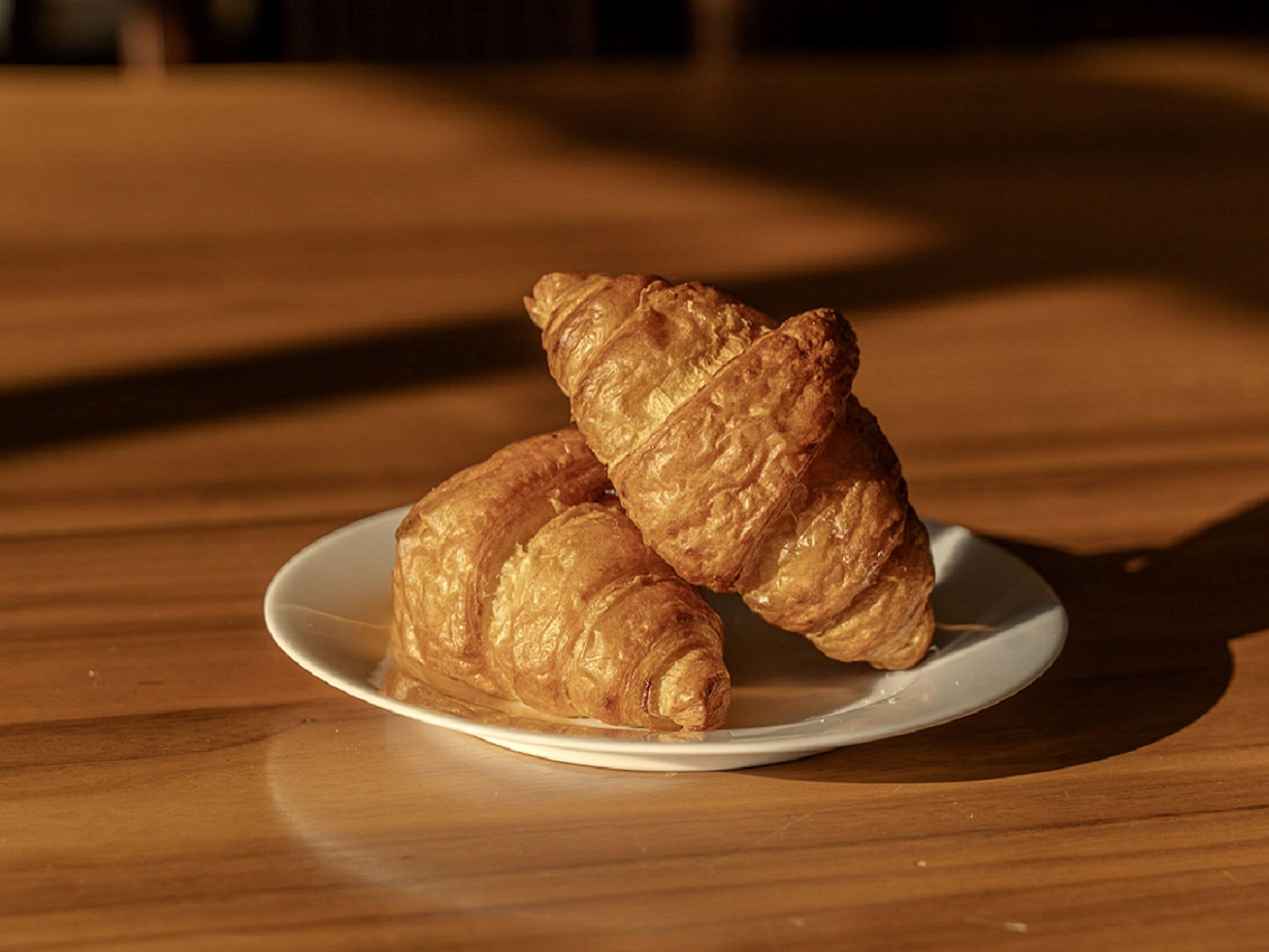 Dois croissants sobre um prato branco em uma mesa de madeira.