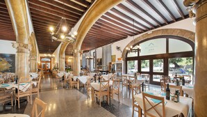Um restaurante espaçoso com altos tetos de madeira e grandes janelas. As mesas estão dispostas com toalhas brancas e cadeiras.