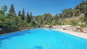 Uma piscina azul límpida cercada por uma cerca de madeira, com um muro de pedra e árvores ao fundo.