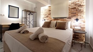 Quarto de hotel com cama, escrivaninha e parede de tijolos.