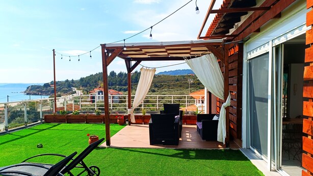 Terraço no telhado com grama artificial, móveis de exterior e vista para o mar.