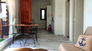 Uma sala de jantar com mesa e cadeiras de madeira, um extintor e vista pela janela.