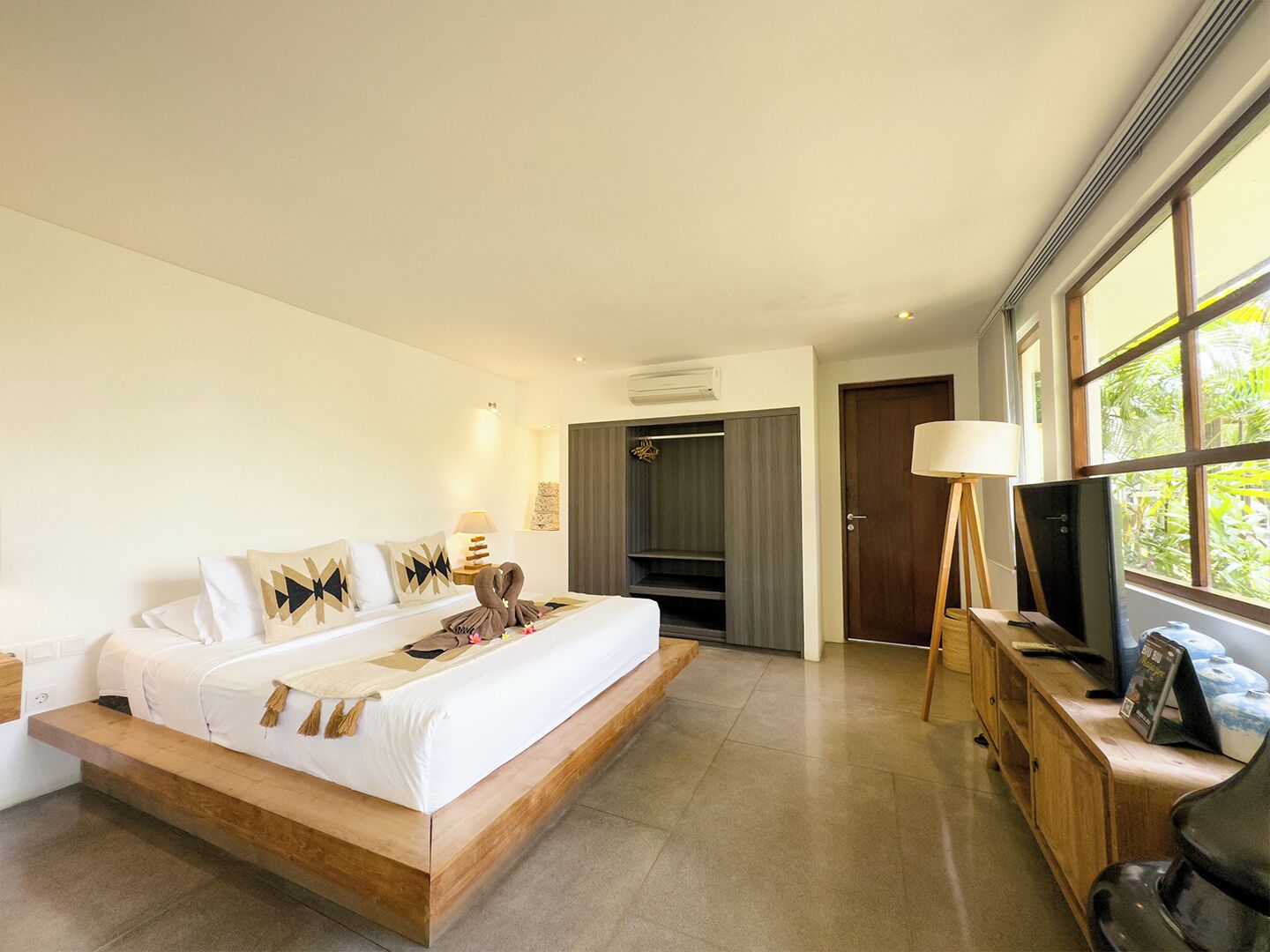 Quarto de hotel moderno com uma cama grande, uma televisão, uma escrivaninha com abajur e um guarda-roupa.