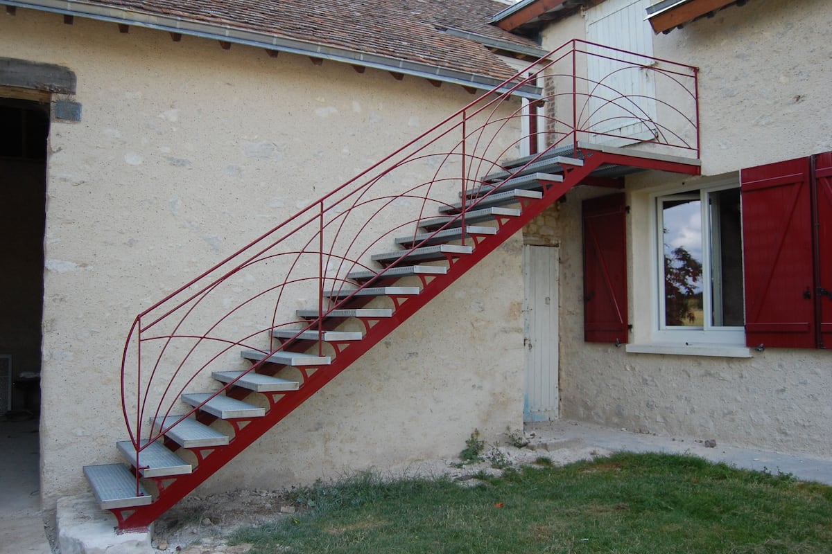 Uma escadaria com corrimãos vermelhos que leva à entrada de um edifício.