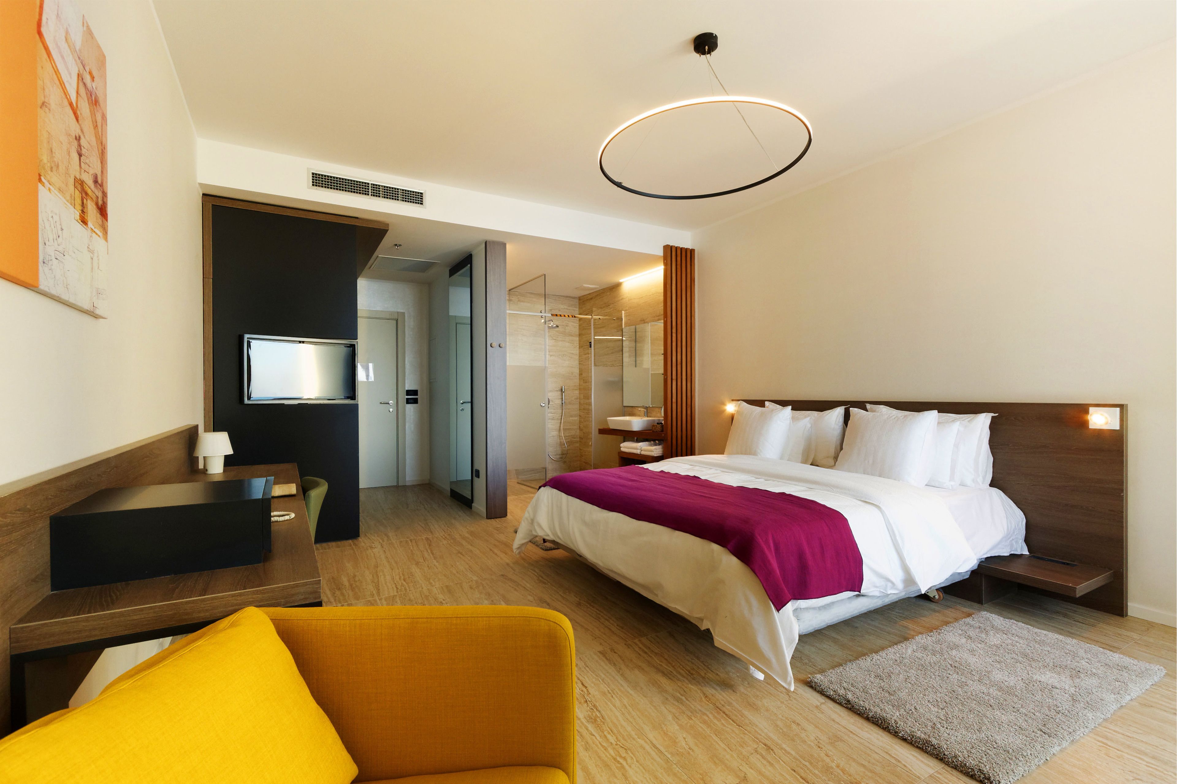 Quarto de hotel moderno com cama, escrivaninha, cadeira, televisão e banheiro.