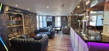 Uma sala de estar moderna com uma parede de destaque em pedra, uma televisão grande e um espaço bar com torneira.