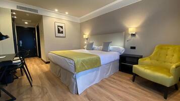 Quarto de hotel com cama, mesas de cabeceira, uma cadeira e uma escrivaninha.