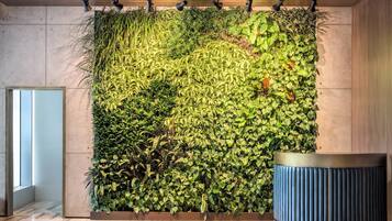 Paredes verticais com diversos vegetais, um contentor cilíndrico de lixo e uma porta com painel de vidro.