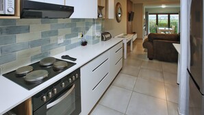 Cozinha moderna com fogão, forno e armários brancos. Há uma área de refeições com mesa e cadeiras.