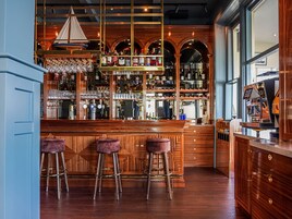 Uma área de bar com banquetas de madeira, adega e máquina de café.