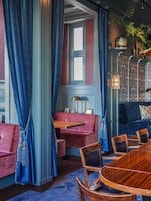Quarto com mesa de jantar de madeira, assentos estofados vermelhos e cortinas azuis.