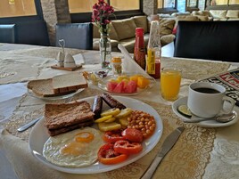 Mesa de café da manhã com torradas, ovos, linguiça, tomate, feijão e uma xícara de café.