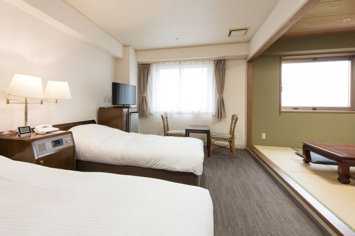 Quarto de hotel com duas camas, televisão, escrivaninha, cadeira e um futon.