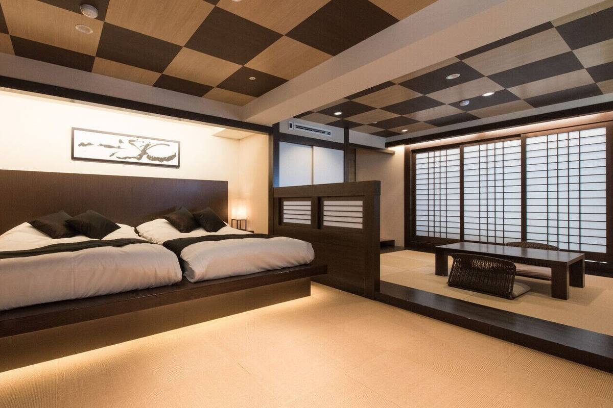 Quarto moderno com cama grande, luminárias laterais, cabeceira de madeira, piso de tatame e vista para o exterior através de biombos shoji.
