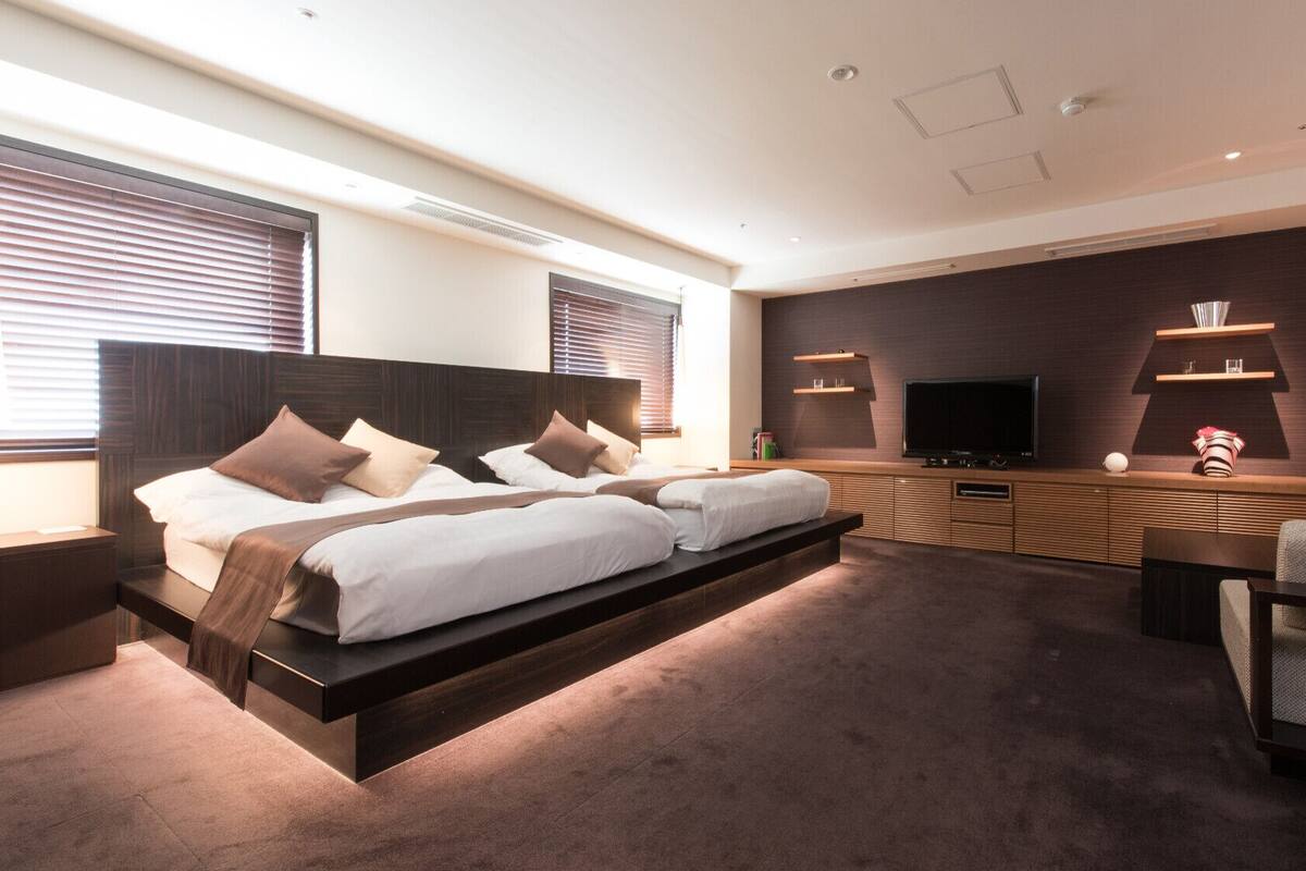 Quarto de hotel moderno com uma cama grande, TV de tela plana, escrivaninha de madeira e nichos embutidos.