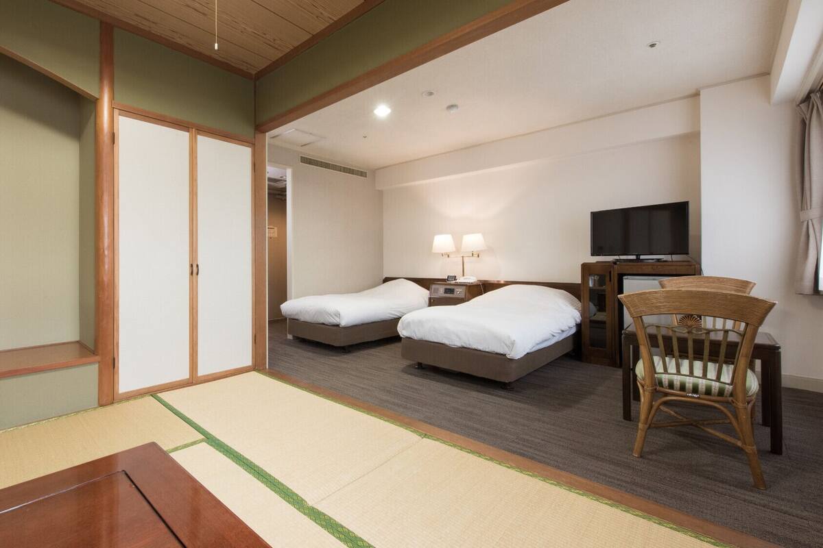Quarto de hotel com duas camas, televisão, escrivaninha e cadeira.