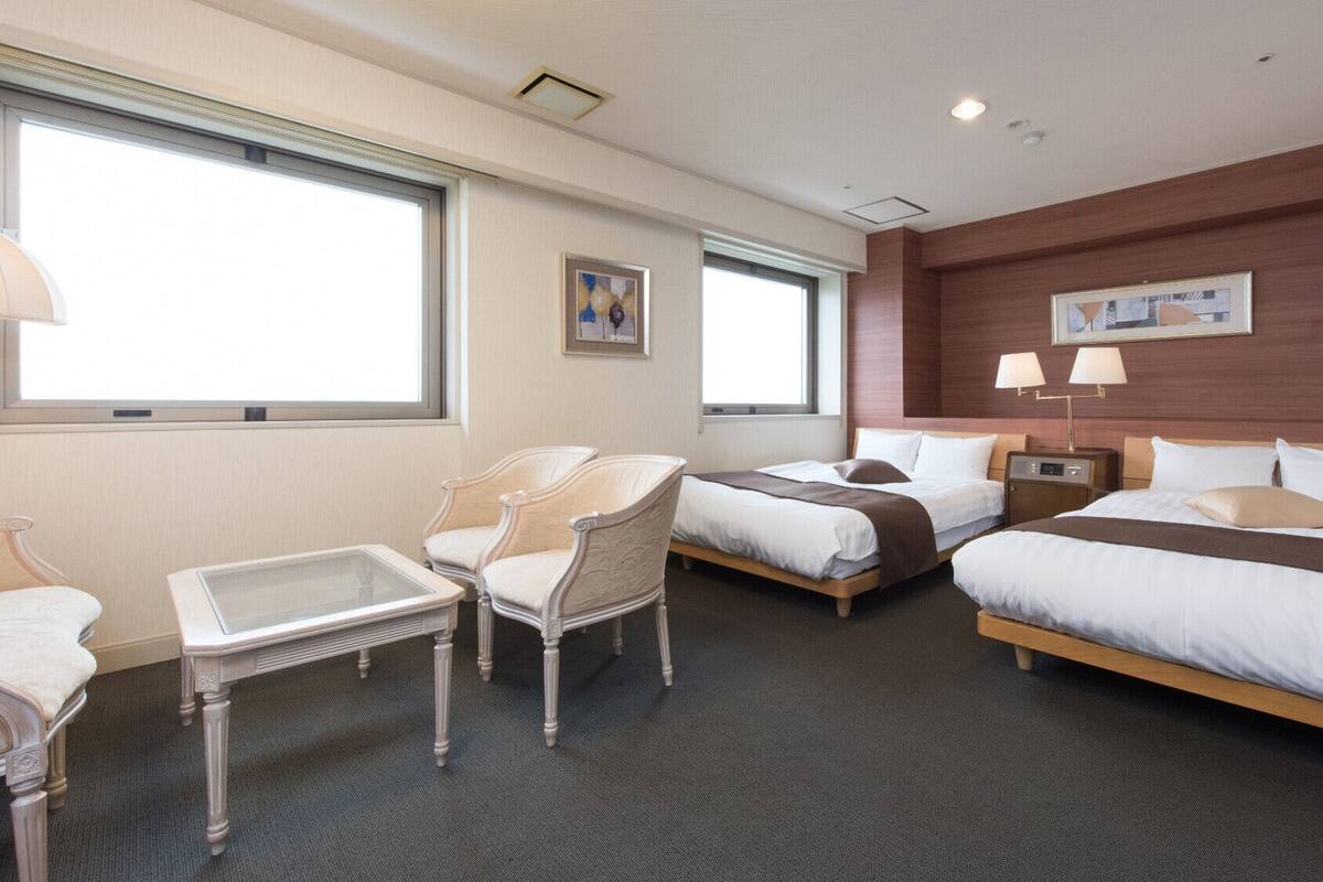 Quarto de hotel com duas camas, uma escrivaninha, uma cadeira e uma mesa pequena.