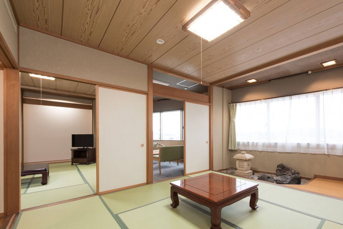 Um quarto japonês tradicional com tatames, uma mesa de madeira baixa, portas de correr e uma grande janela com cortinas.